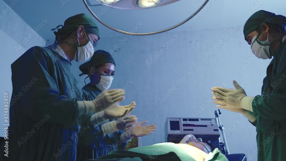 Group of surgery doctors in sterile gloves and protective face masks standing applause by ...