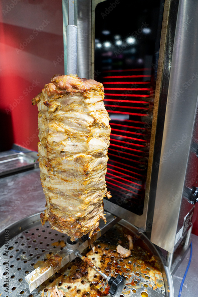 Rotating skewered chicken meat grilled in stainless steel grill and ...