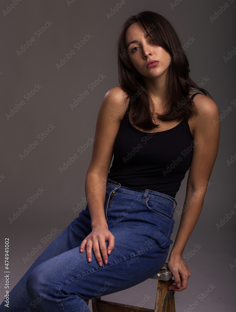 Fashion model sit on chair in a blu jeans and black undershirt barefoot ...