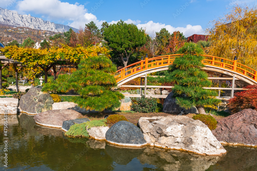 Pond and banks of stones and a yellow bridge in a Japanese-style garden ...