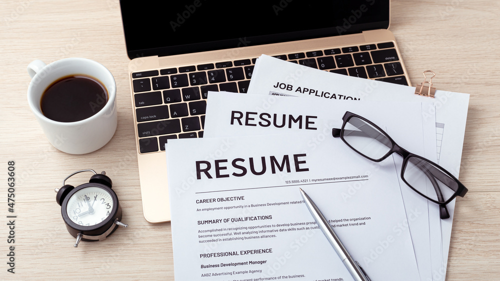 Resume and job application documents on laptop with glasses and pen ...