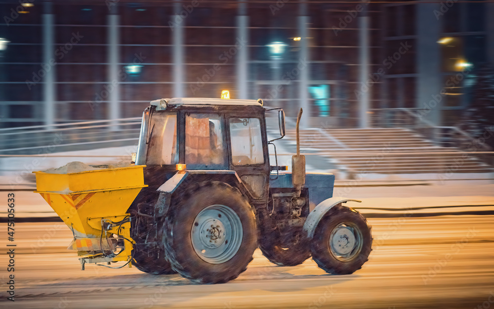 Tractor with mounted salt spreader drive on city road at night during ...