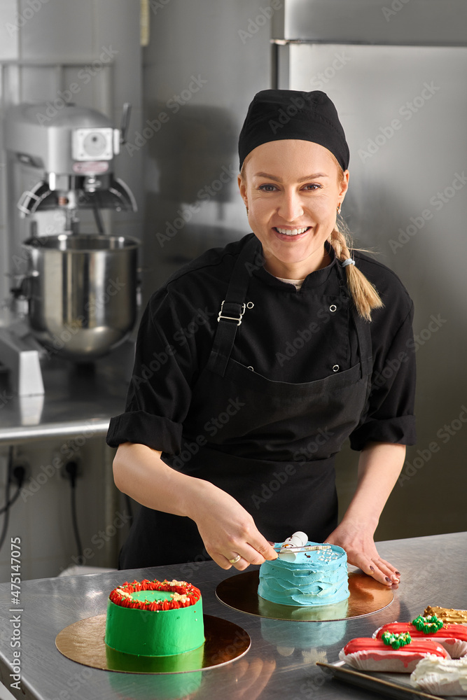Beautiful and cute girl smiling and decorating cake. Young confectioner ...