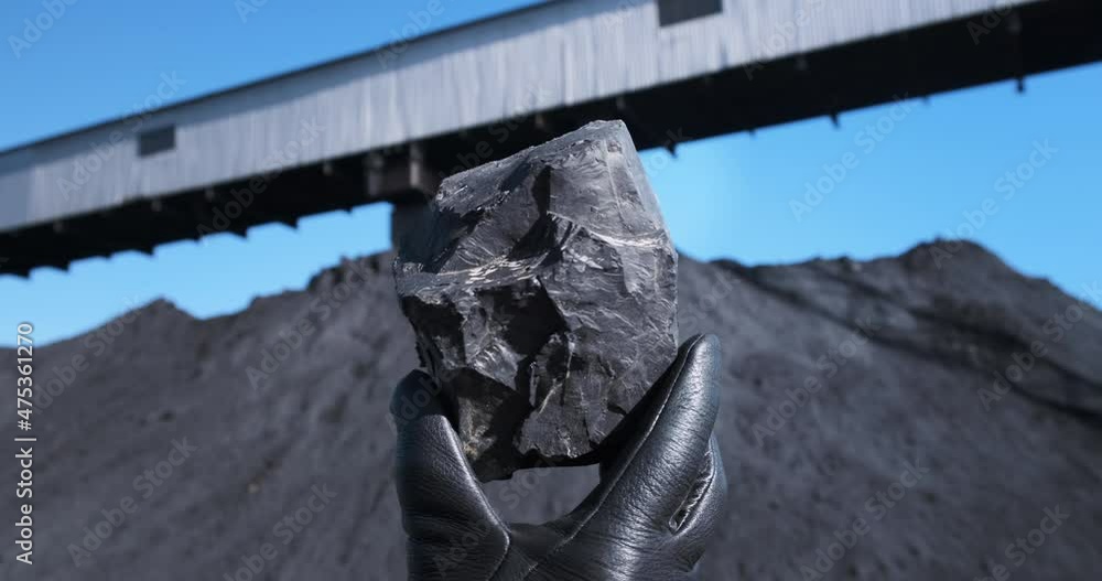 Close-up, coal piece in man's hand backdrop of black mineral pile ...