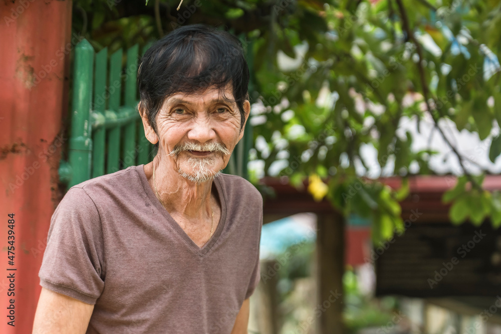 A friendly old Filipino man in his 70s in front of his rural home ...