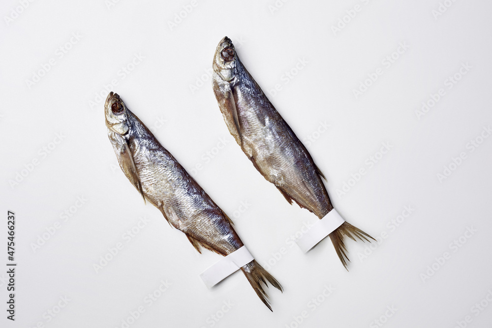 Two salted sun-dried sabrefish with paper labels on tails on white ...