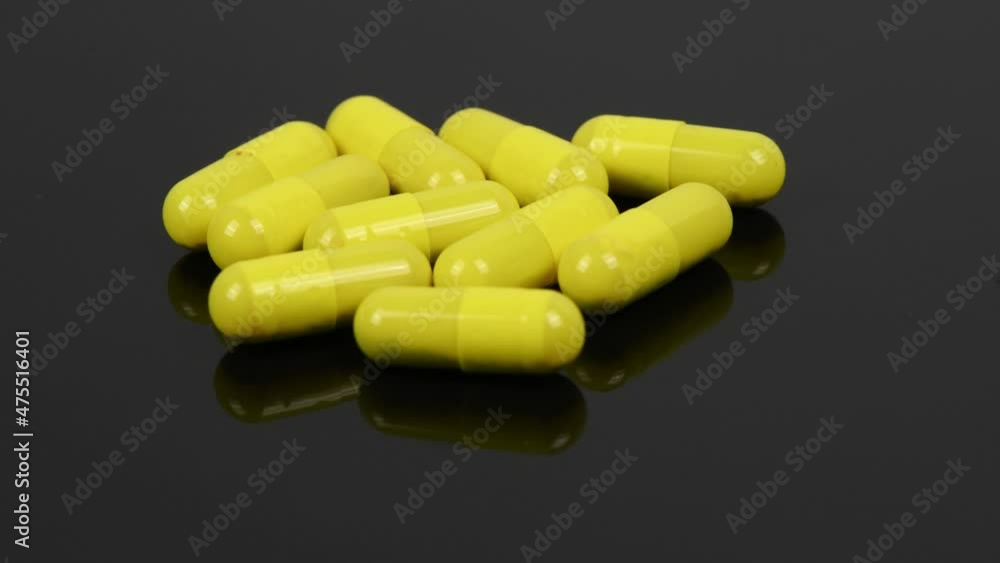 Yellow capsules on black acrylic background. Side view. Loop motion ...