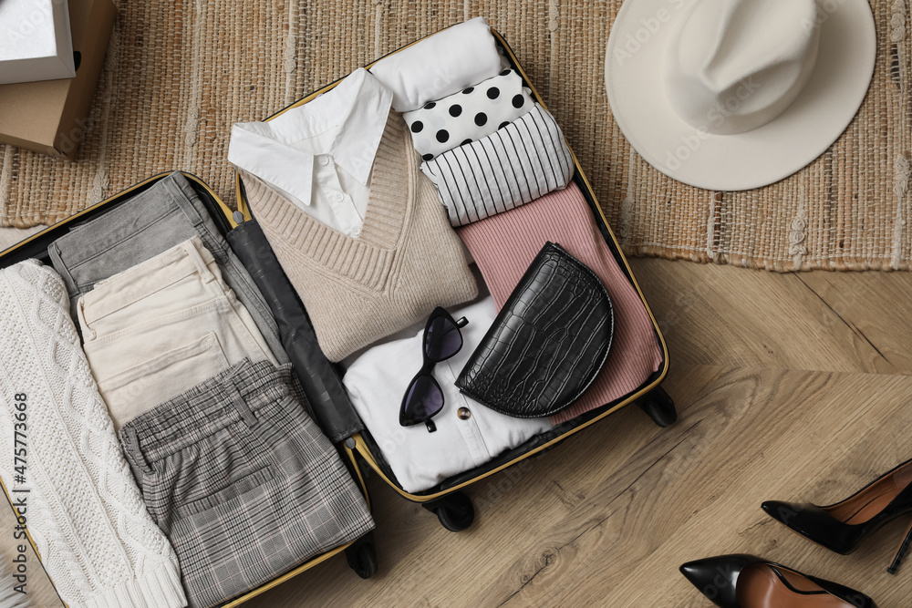 Open suitcase with folded clothes, accessories and shoes on floor, flat ...