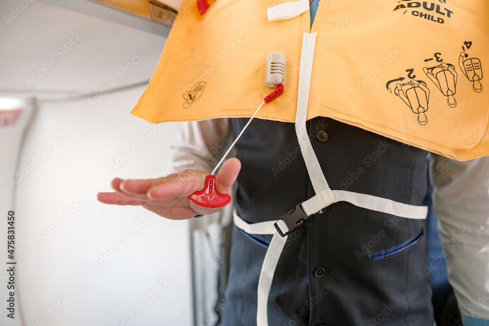 Man flight attendant demonstrating how to use life vest in airplane ...