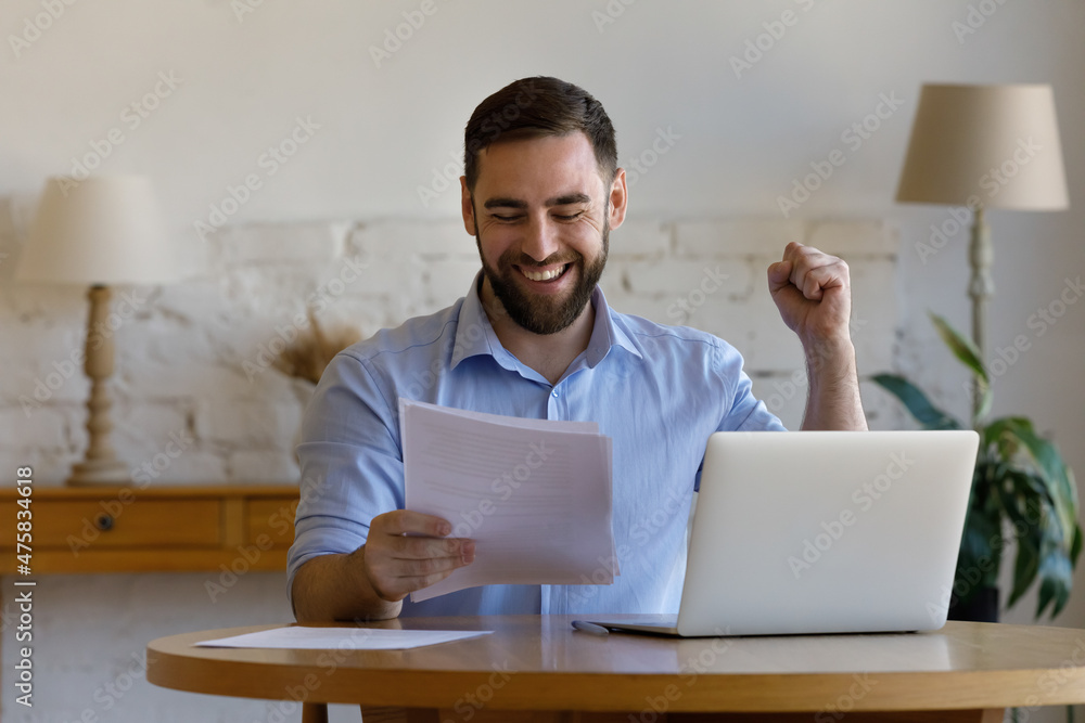 Emotional laughing happy young man looking at paper document, feeling ...