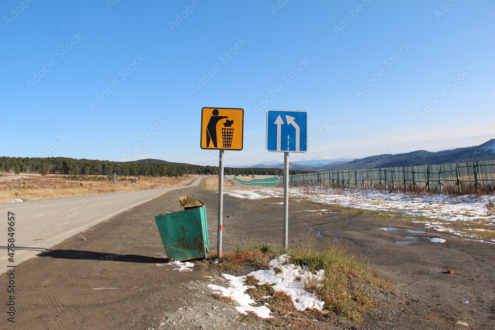 Trash can and road signs near the highway. Autumn landscape with ...