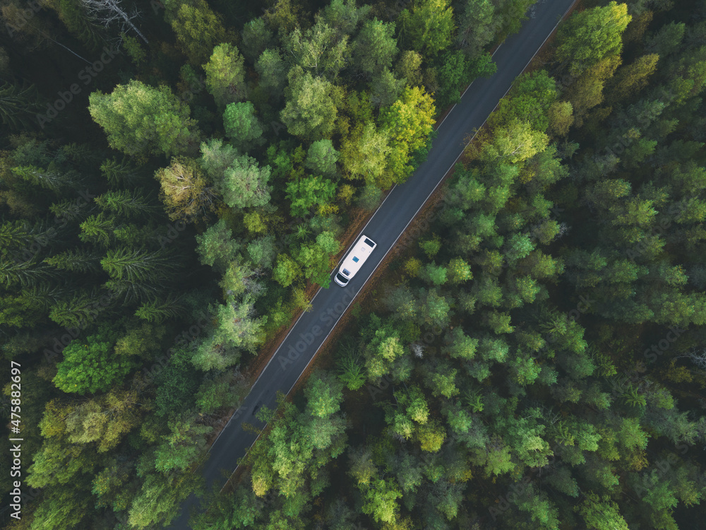 White camper van with solar panels drive through green forest. Aerial ...