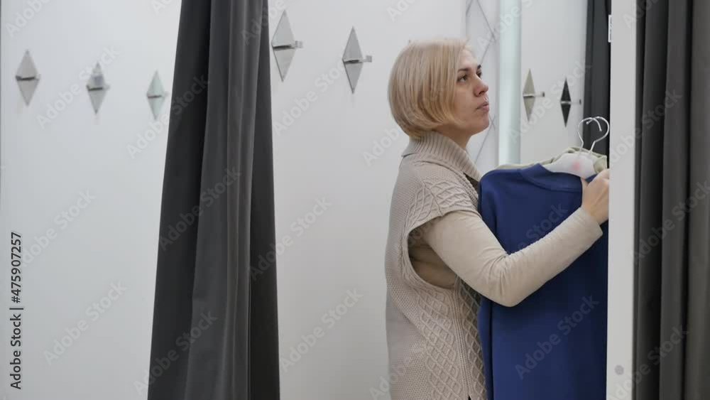 A young Caucasian woman in a boutique walks into a fitting room to try ...