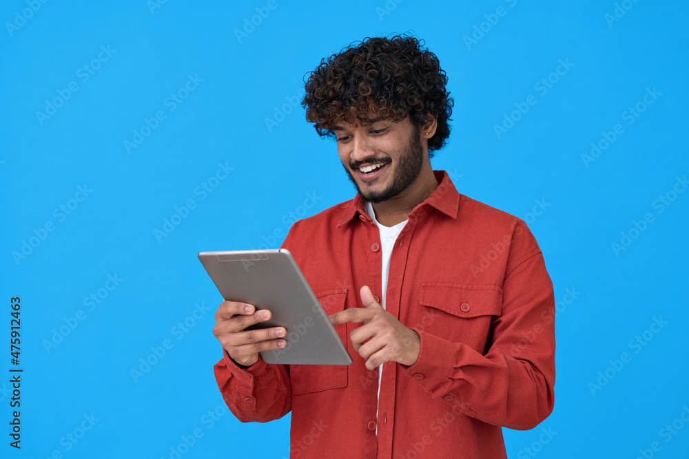 Happy indian young man using digital tablet isolated on blue background ...