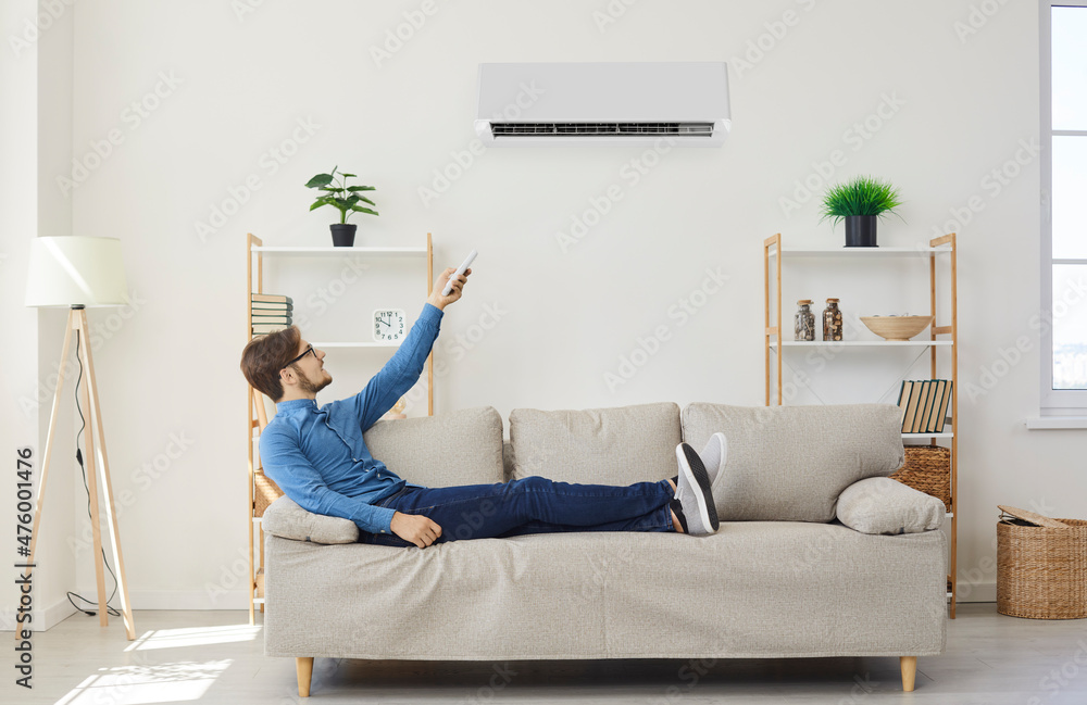 Foto de Happy man resting on couch under air conditioner enjoys fresh ...