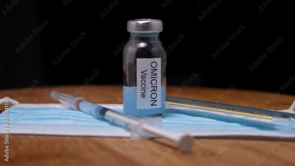 Ampoule with Omicron vaccine, thermometer, syringe and medical mask on ...