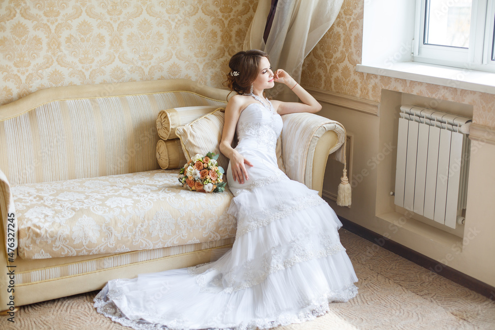 Beautiful young Bride with classic hairstyle sits on a sofa in a ...