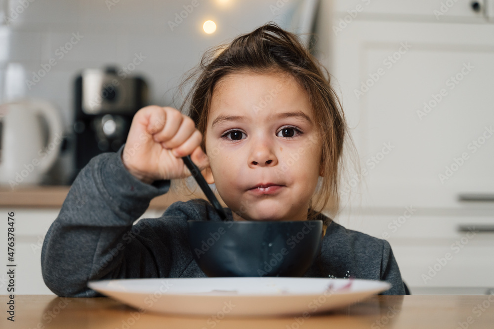 Beautiful child girl eats soup from black bowl with bread and onion ...