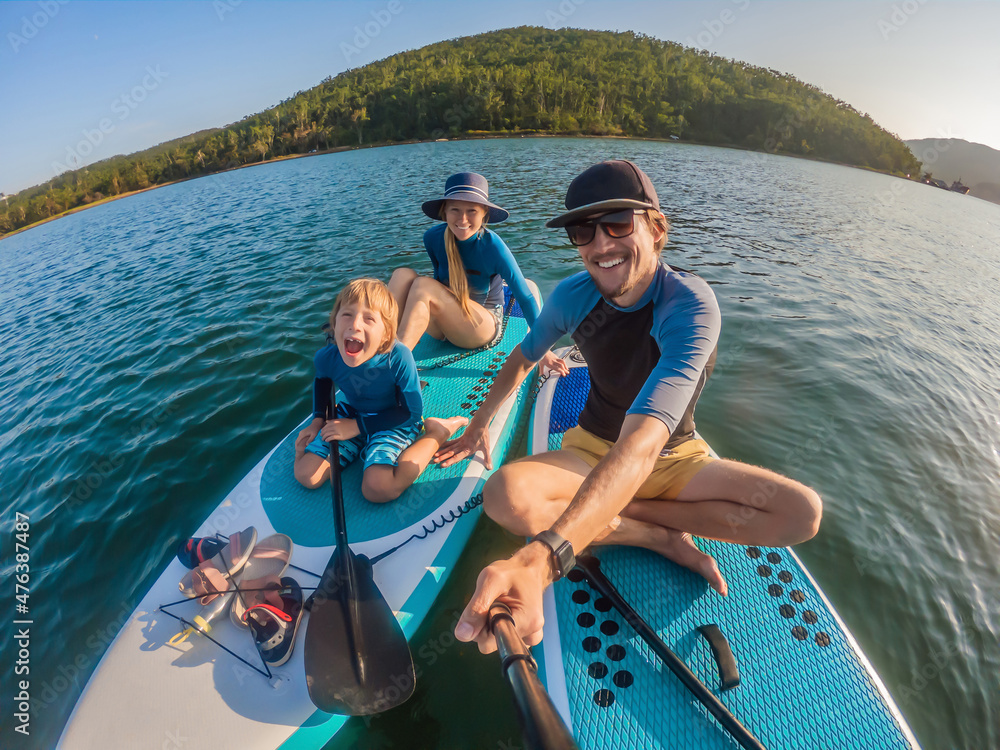 happy family of three, dad, mom and son, enjoying stand up paddling ...