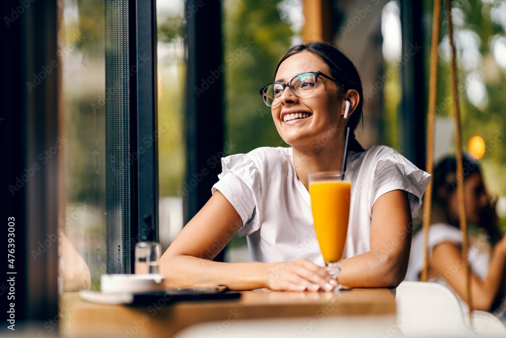 A happy student sits in a cafe, having fresh orange juice, listening to ...