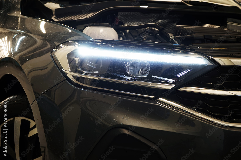 A close-up shows the front of a modern car. Headlight in focus. Stock ...