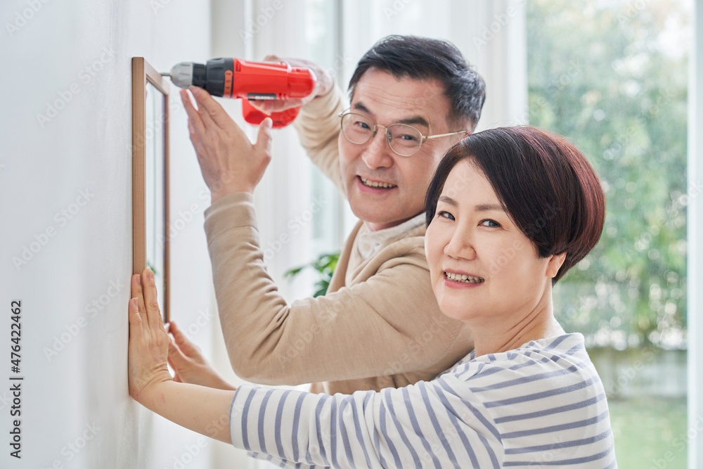 Middle-aged couple trying to hang a picture frame with a drill on the ...