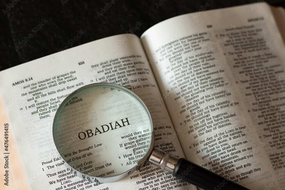 Obadiah prophet open Holy Bible Book with a magnifying glass on dark ...