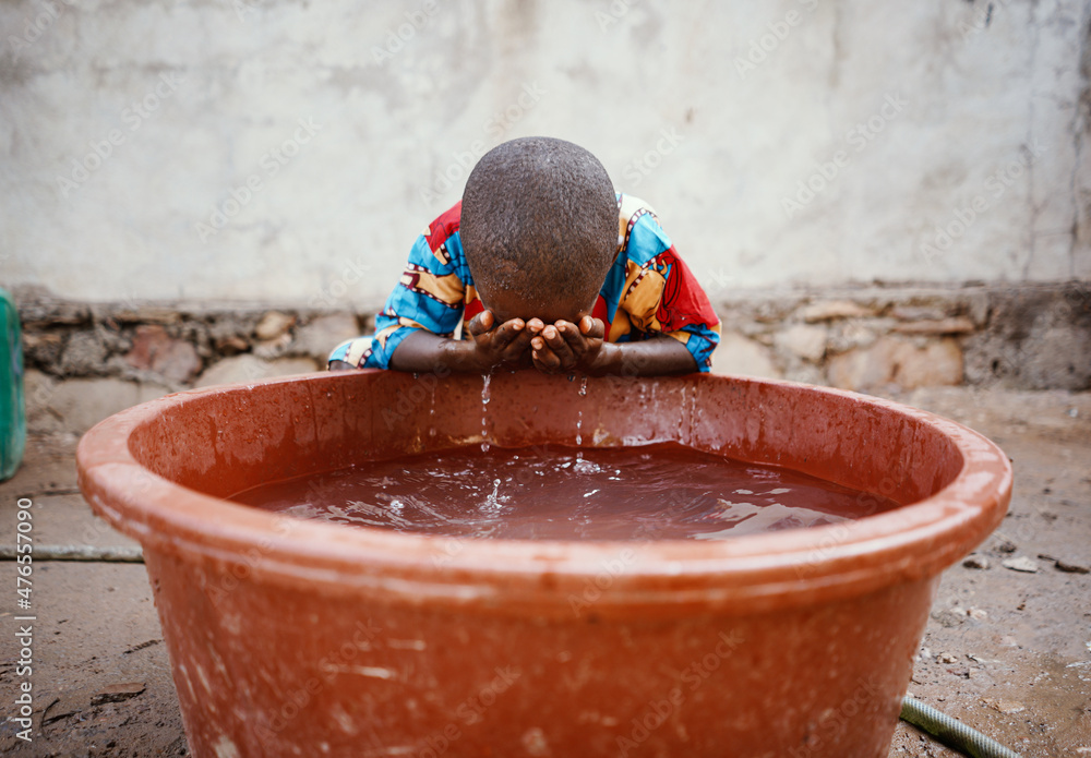 Little black african boy washing his face over a huge brown plastic ...