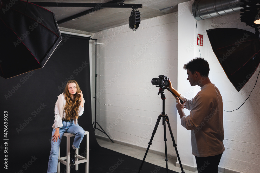 Male taking photo of female sitting on chair in professional studio ...