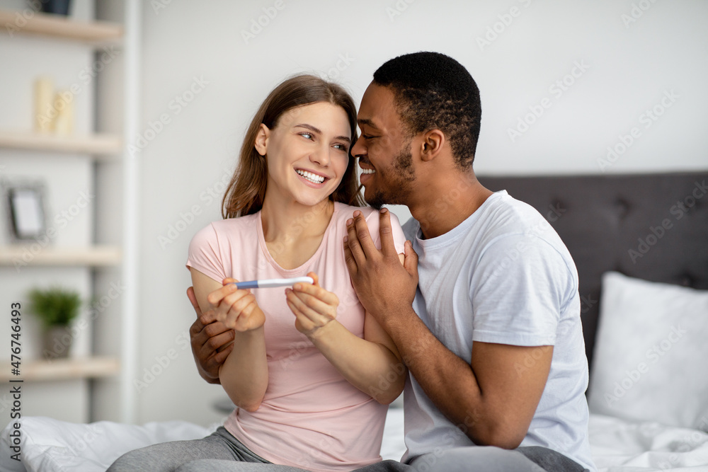 Excited multinational couple with positive pregnancy test hugging on ...
