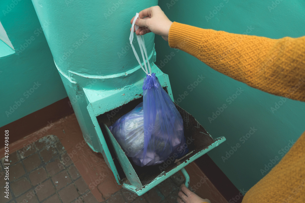 A woman's hand with a garbage bag opens the hatch of the garbage chute ...