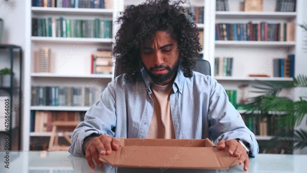 Unhappy young Indian man frustrated by received parcel unpacking box ...