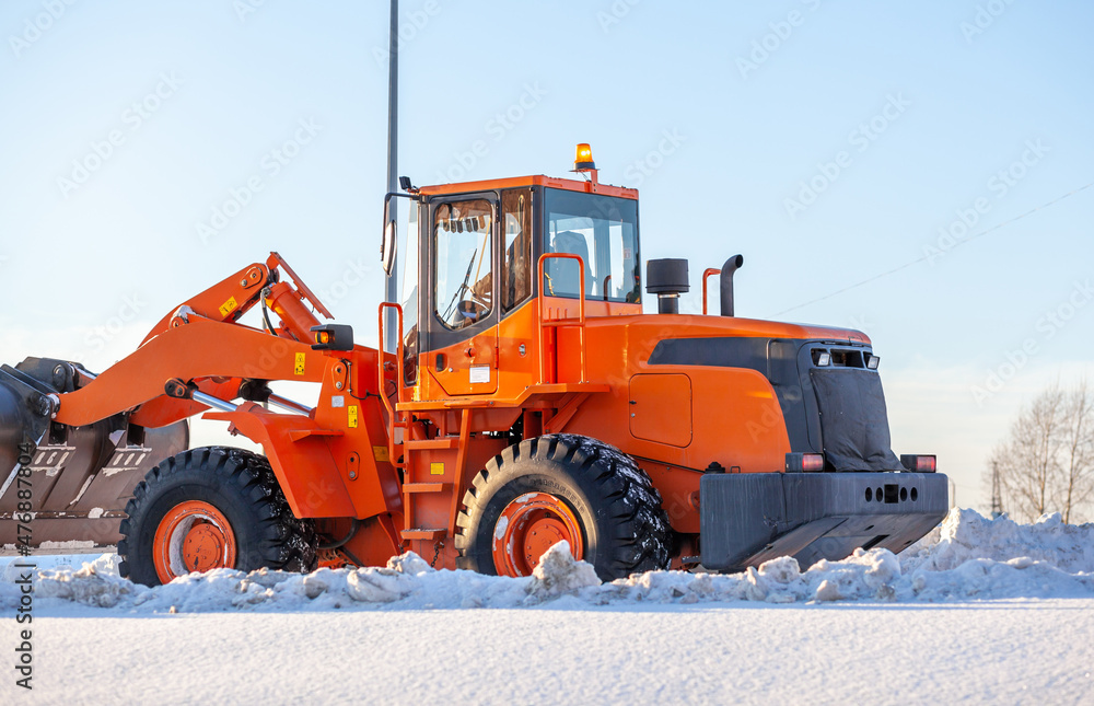 Big orange tractor cleans up snow from the road and loads it into the ...