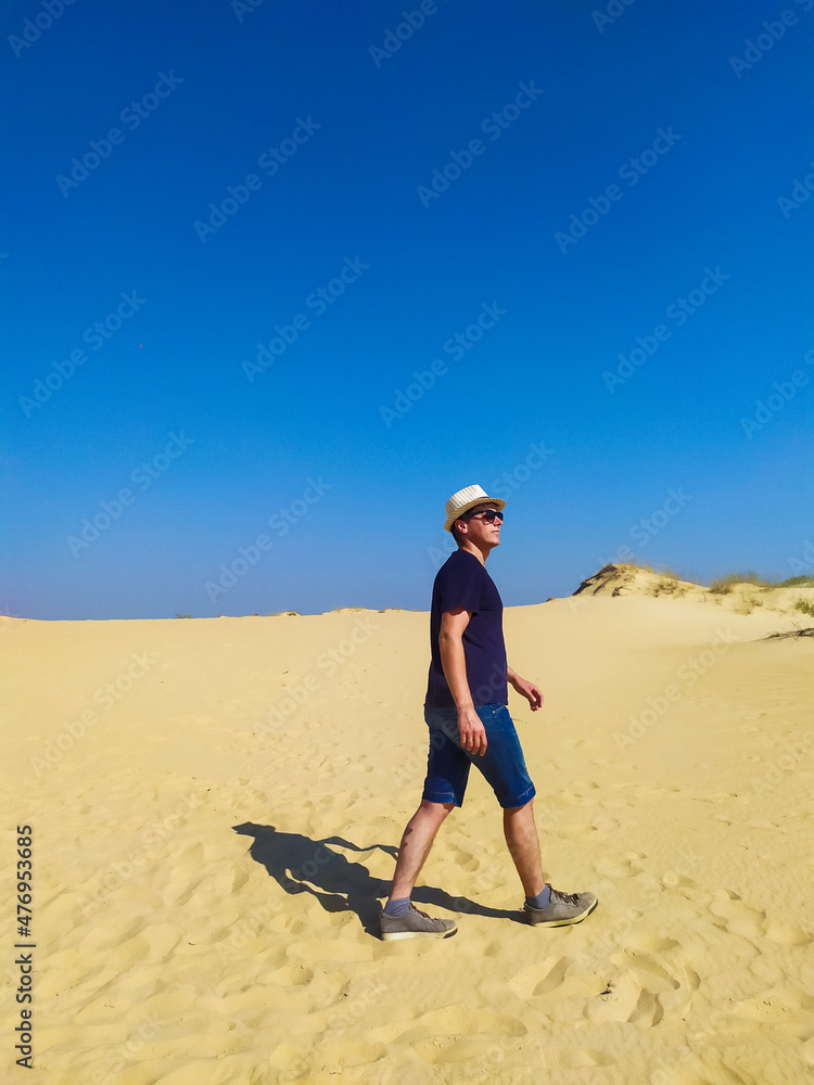 Young woman in white blouse and brown shorts going in desert under blue ...
