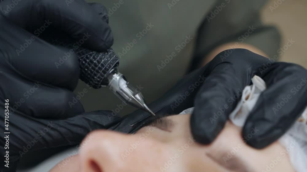 The master makes permanent eyebrow makeup with a needle tattoo machine ...