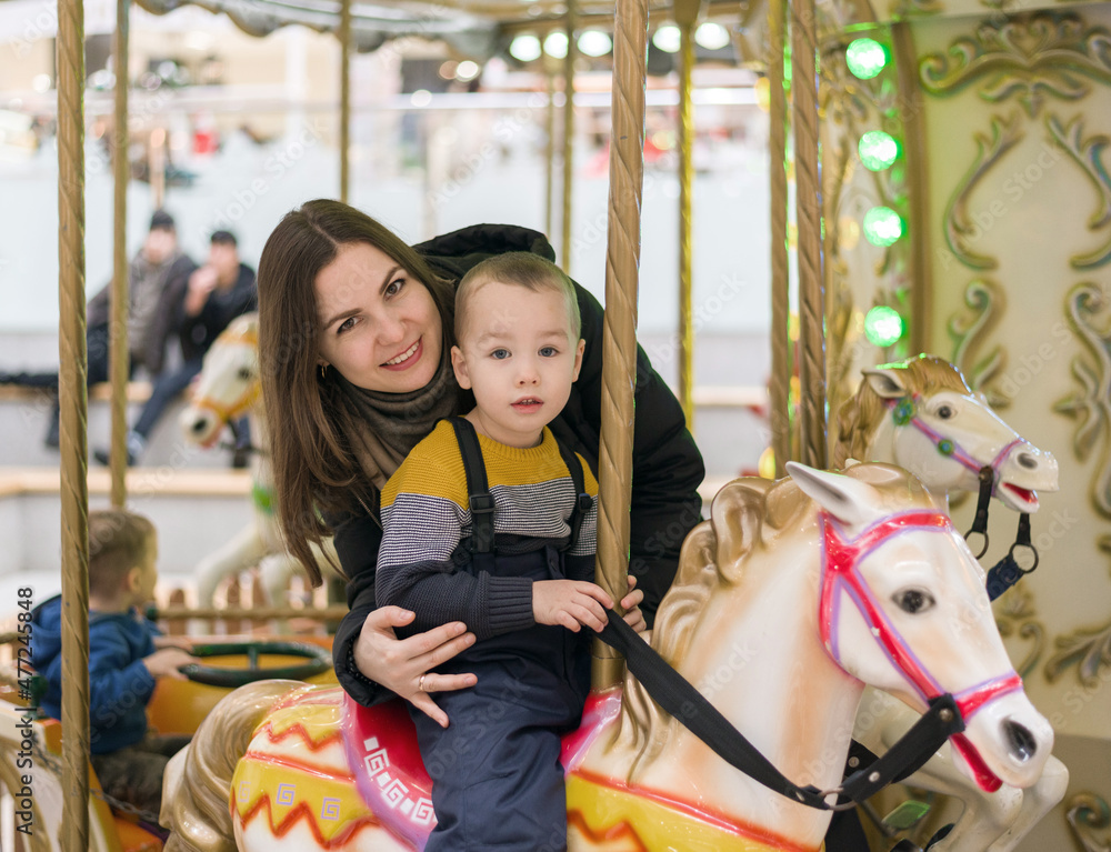 Mom and son are having fun on the merry-go-rounds. Child boy rides a ...