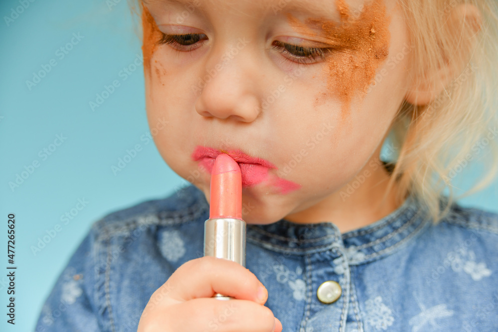 The little girl took the makeup from her mother and paints her lips ...