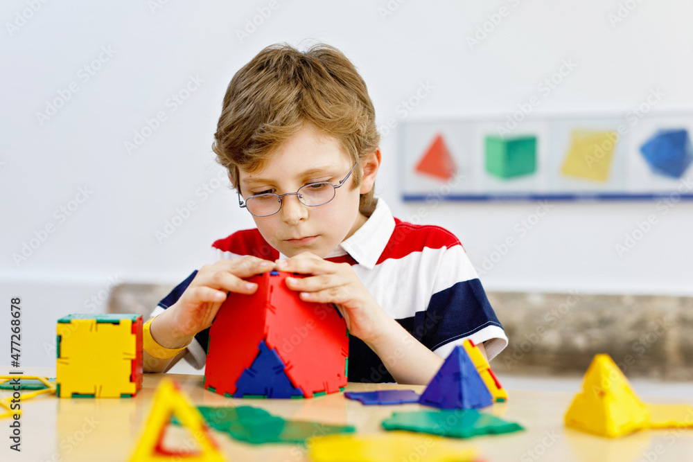Little kid boy with glasses playing with lolorful plastic elements kit ...