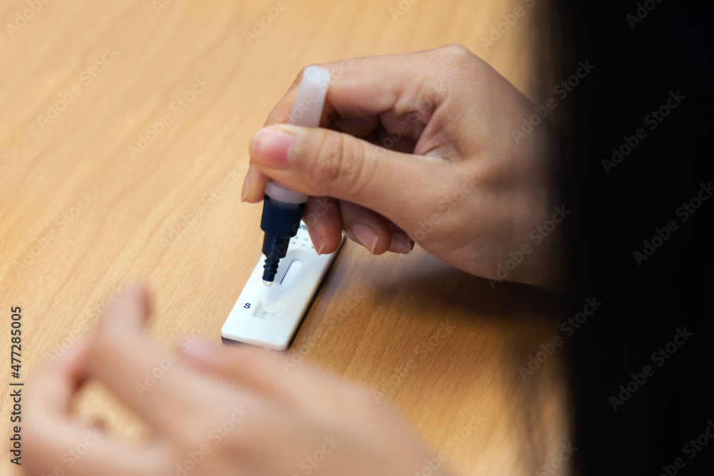 Close-up hand holding buffer and drop mucus sample placed on strip of ...