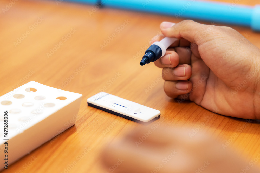 Close-up hand holding buffer and drop mucus sample placed on strip of ...