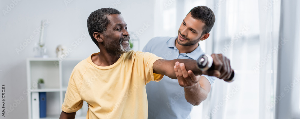 young physiotherapist assisting smiling african american patient ...