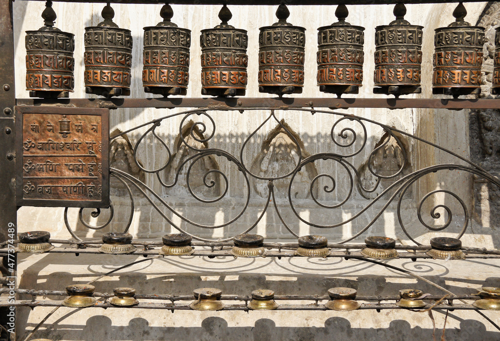 Prayer wheels and butter lamps stand next to the large white Swayambhu ...
