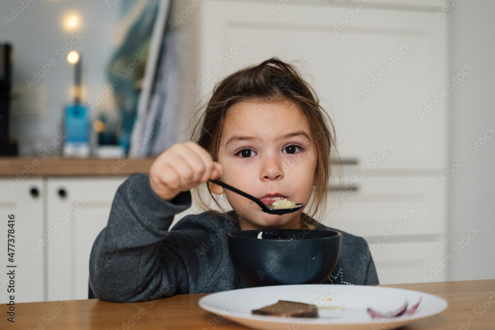 Beautiful child girl eats soup from black bowl with bread and onion ...