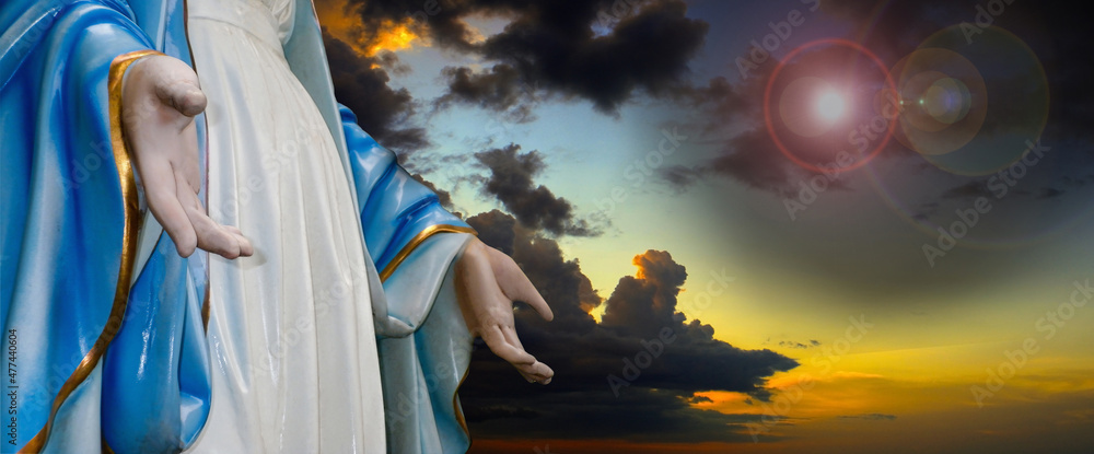 Hand of Saint Mary statue with lens flare effect on dramatic cloud sky ...