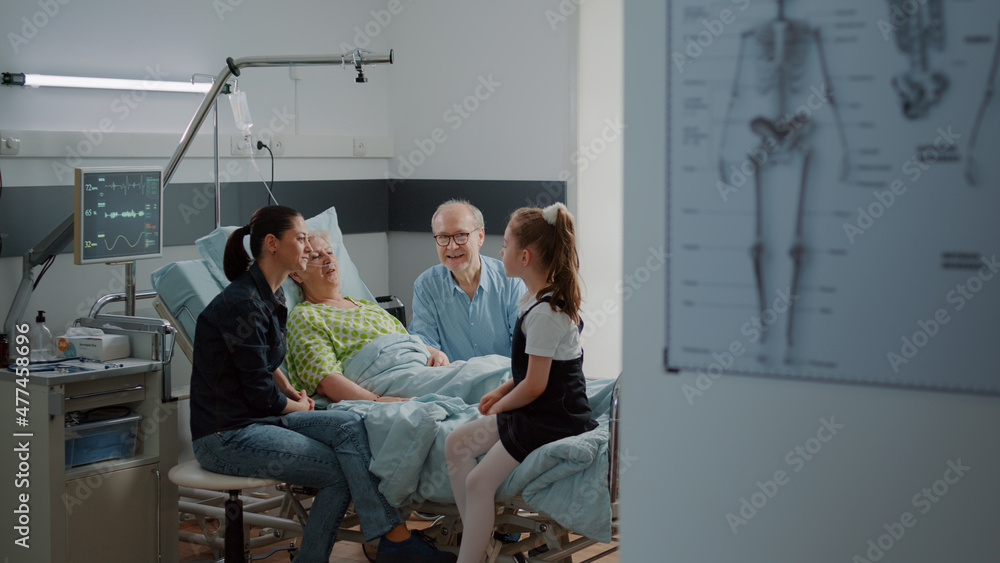 Young girl visiting aged woman in hospital ward bed with mother and old ...
