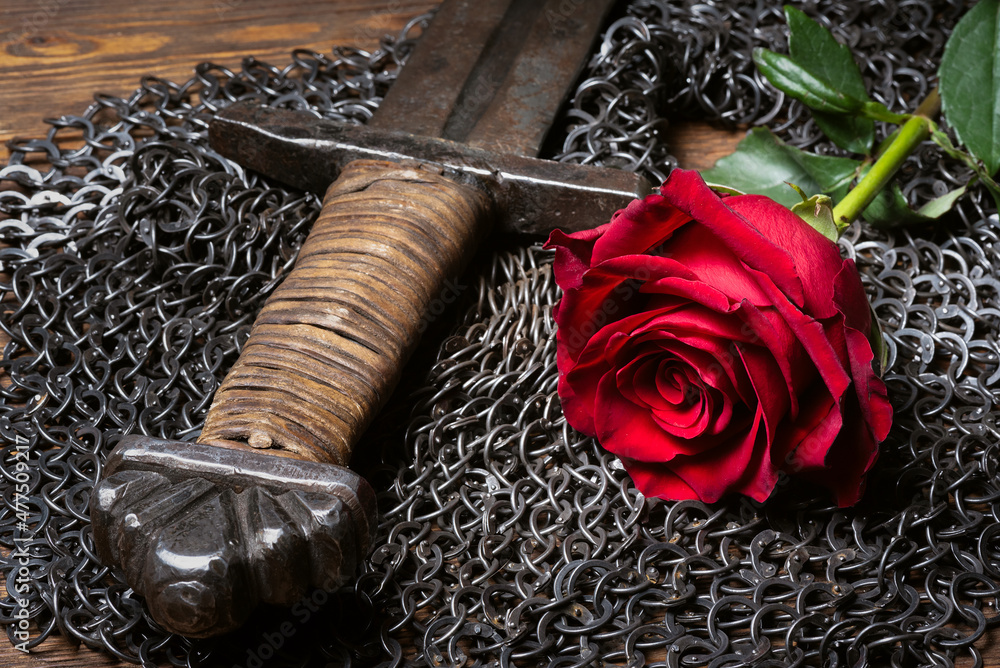 Red rose flower and knight sword on the black table background close up ...