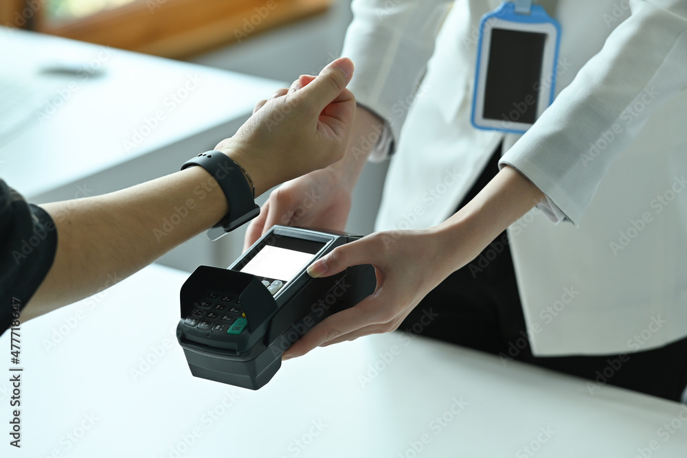 Cropped image of a young man using a smartwatch for doing a payment at ...
