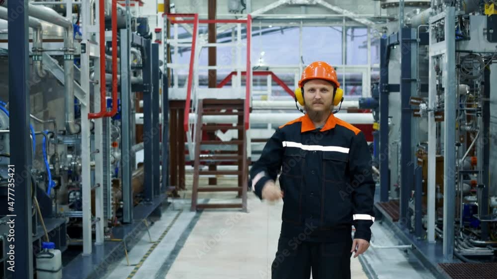 A plant worker in a hard hat and earphones stands in a gas compression ...