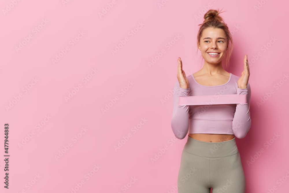 Smiling slim woman does workout with resistance band performs exercises ...