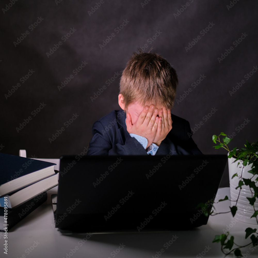 A sad boy in a school suit is crying at the computer, copy space on a ...